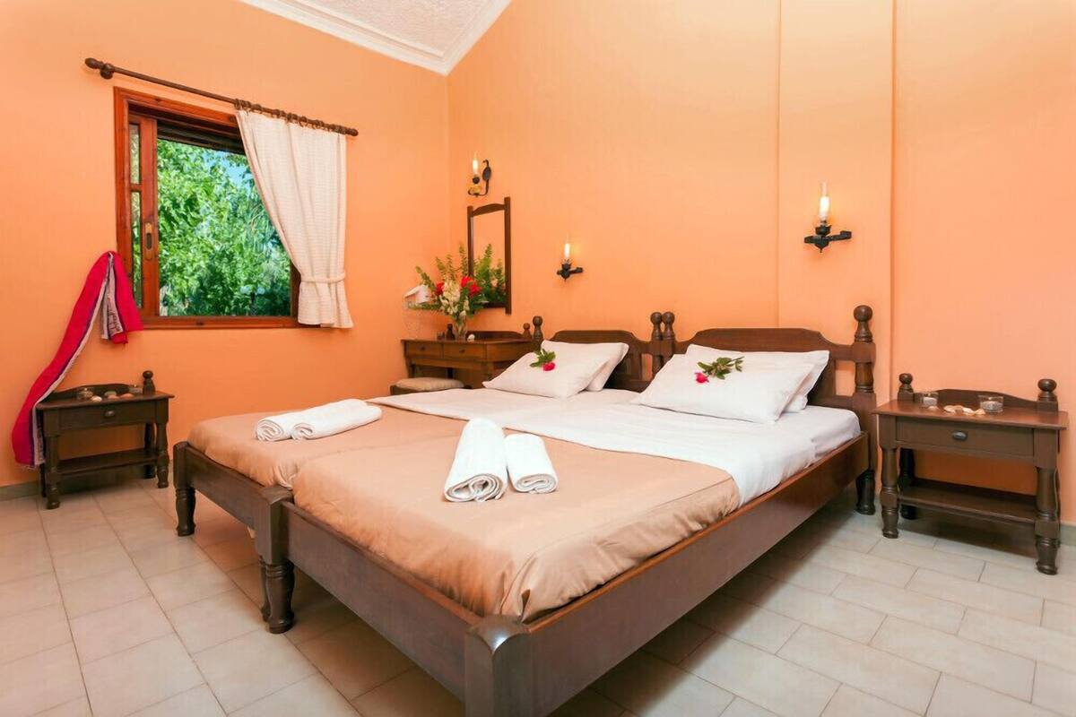Quarto com uma cama grande, duas mesas de cabeceira, um criado-mudo, uma janela com cortinas e um espelho na parede.
