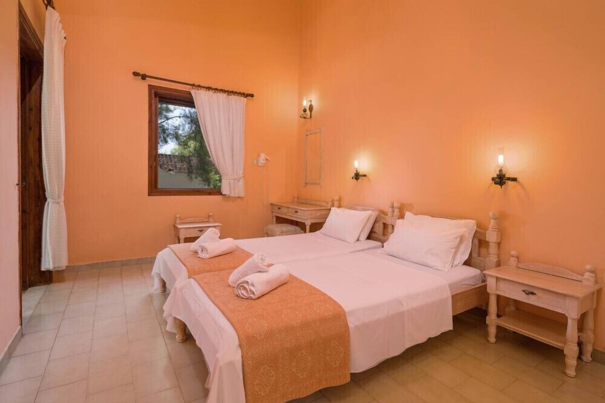 Quarto com duas camas, janela com cortinas, luminárias de cabeceira e mesa de cabeceira de madeira.
