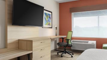 Quarto de hotel com escrivaninha, cadeira, cama, janela com vista e ar condicionado.