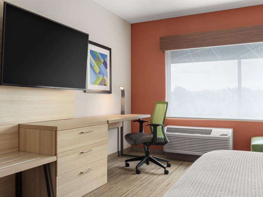 Quarto de hotel com escrivaninha, cadeira, cama, janela com vista e ar condicionado.
