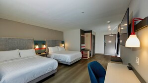 Quarto de hotel com duas camas, uma escrivaninha, uma cadeira e banheiro visível por uma porta aberta.