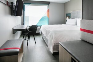Quarto de hotel com cama, escrivaninha, cadeira e um banco.