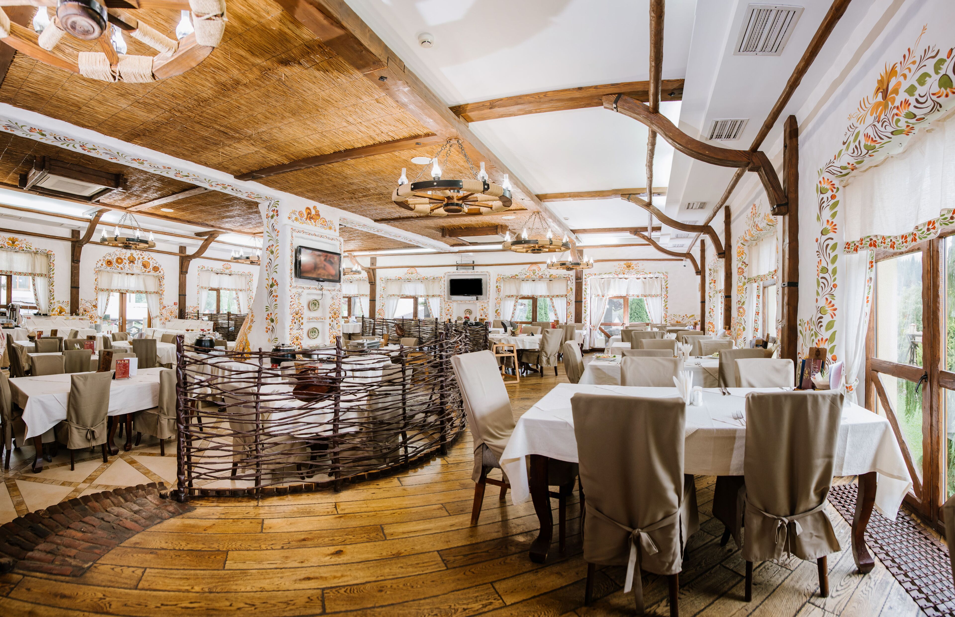 Restaurante com vigas de madeira, paredes brancas e área de estar central com mesas e cadeiras.