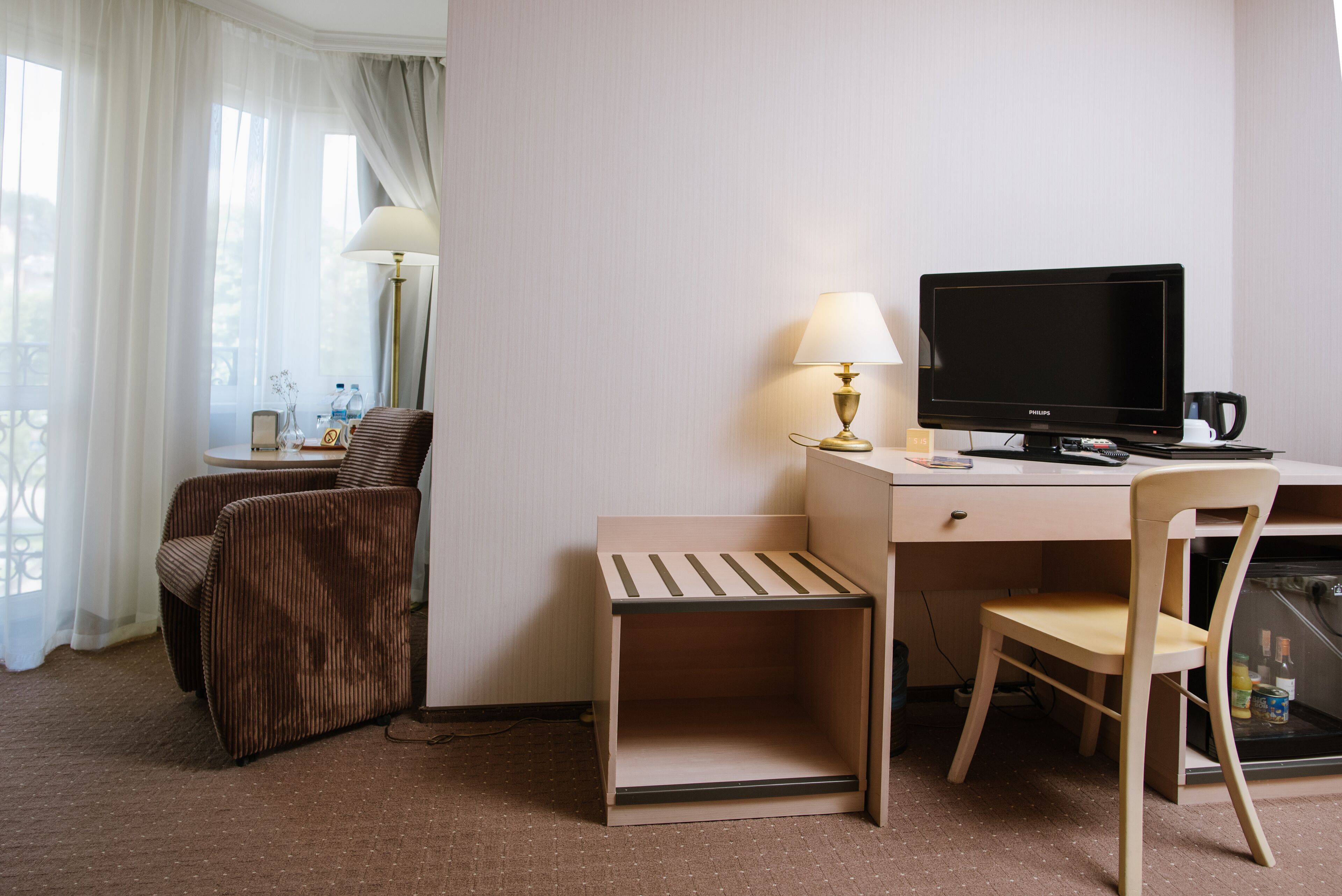 Quarto de hotel com escrivaninha, computador, cadeira, luminária e mesinha de centro com um vaso e porta-retrato.