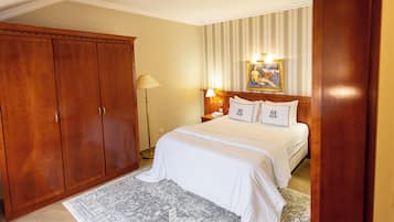 Quarto de hotel com um guarda-roupa de madeira grande, uma cama com roupa de cama branca, uma cortina listrada e um quadro sobre a cama.