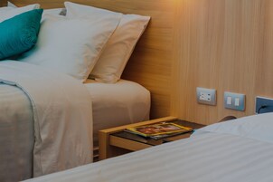 Quarto de hotel com uma cama, uma mesa de cabeceira com uma revista e uma tomada na parede.