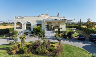 Hotel City Gate com design moderno, destacando uma entrada imponente, área de estar coberta ao ar livre e um estacionamento com carros.