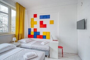 Quarto de hotel com duas camas, uma escrivaninha, uma televisão e uma obra de arte colorida na parede.