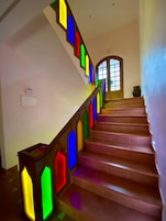 Uma escadaria com painéis de vitrais coloridos nas grades e corrimão de madeira.
