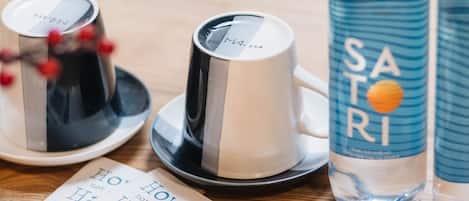 Uma mesa de madeira com duas máquinas de café metálicas, uma garrafa de água e um guia de viagens.