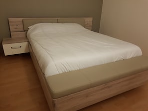 Uma cama com estrutura de madeira e colchão bege.