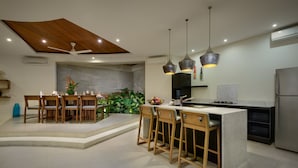 Cozinha moderna com ilha central, banquetas, cadeiras de madeira, iluminação pendente e ventilador de teto.