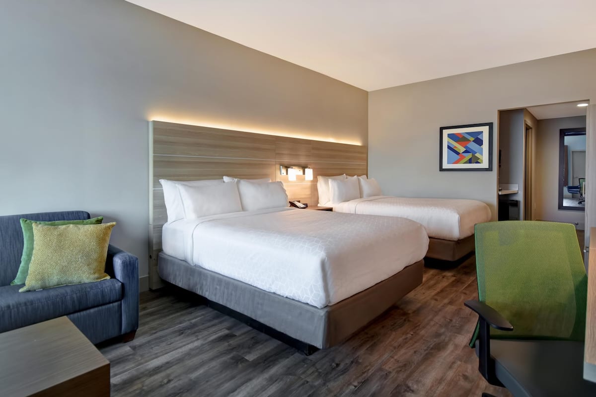 Quarto de hotel com duas camas, um sofá, uma escrivaninha e uma cadeira.