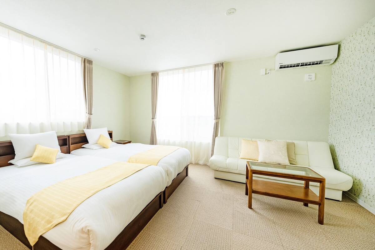 Quarto de hotel com uma cama grande, um sofá, uma mesa de centro e um ar condicionado.