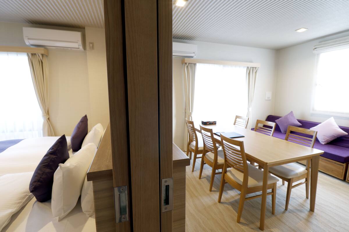 Quarto de hotel com cama, mesa de madeira, cadeiras, sofá e janela.
