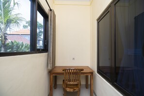 Quarto de canto com mesa e cadeira de madeira, uma janela grande e vista para um prédio e palmeiras.