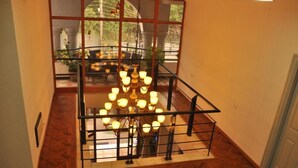 Escadaria com corrimão, um candelabro e vista para uma varanda com plantas e uma mesa.