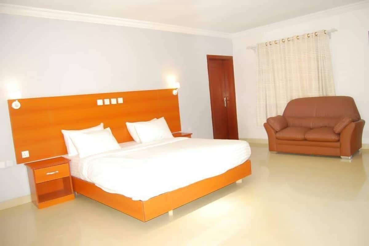 Quarto com cama, mesa de cabeceira e poltrona marrom.