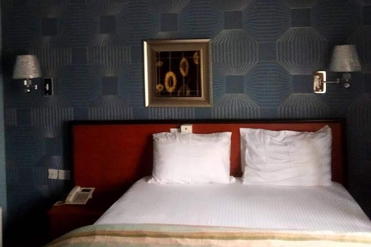 Quarto de hotel com cama, duas luminárias de cabeceira, um quadro na parede e telefone na mesinha de cabeceira.