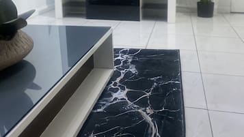 Uma sala de estar moderna com uma TV de tela plana em um suporte branco, uma mesa de centro de mármore, uma planta em vaso e flores de orquídea brancas.