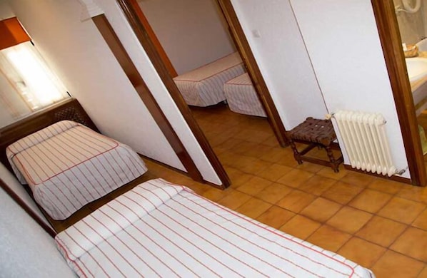 Quarto pequeno e compacto com duas camas, um radiador e um banquinho.