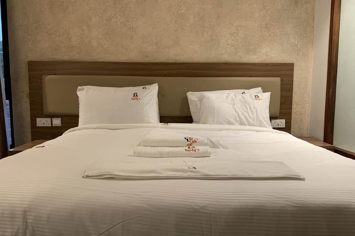 Uma cama bem arrumada com lençóis e almofadas brancas, cabeceira de madeira e uma mesinha com abajur ao lado da cama.