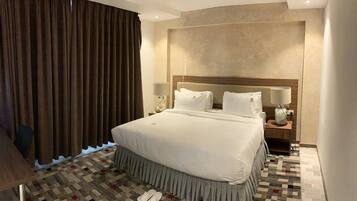 Quarto de hotel com uma cama grande, mesa de cabeceira com abajur e um tapete estampado.
