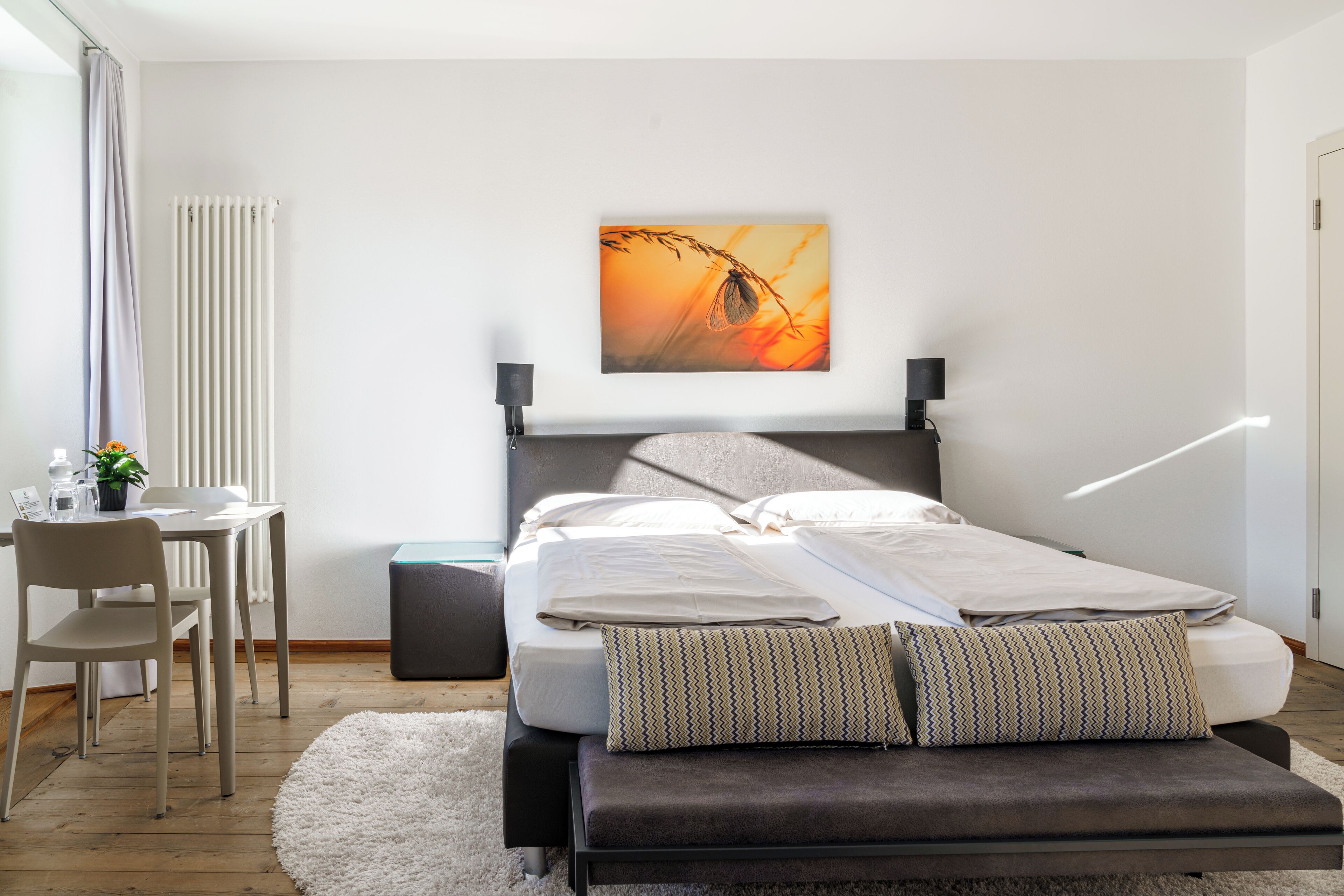 Quarto moderno com cama, mesa de cabeceira, cadeira e uma obra de arte na parede.