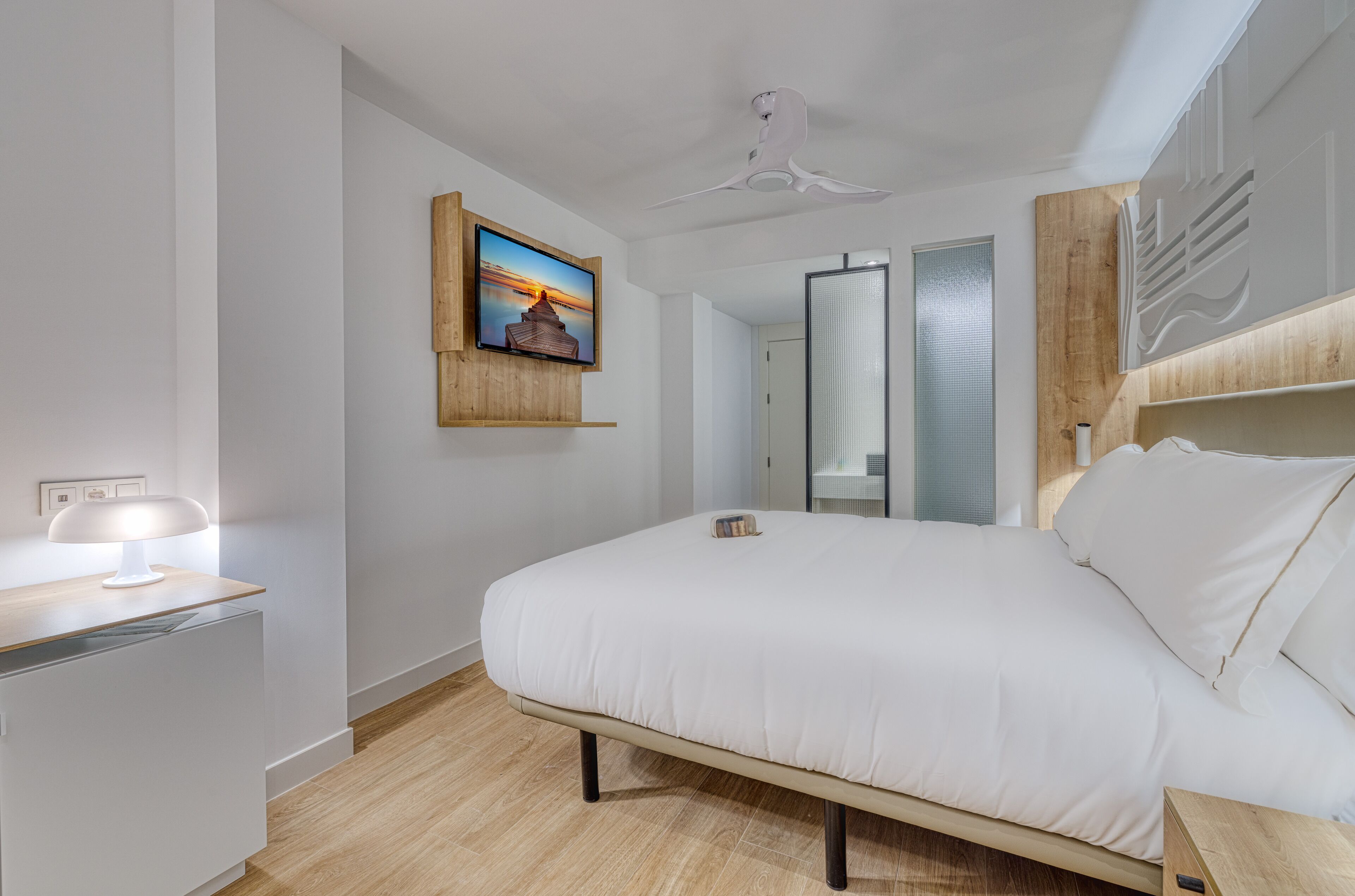 Um quarto moderno com uma cama grande, uma TV na parede, um ventilador de teto e uma cabeceira de madeira.