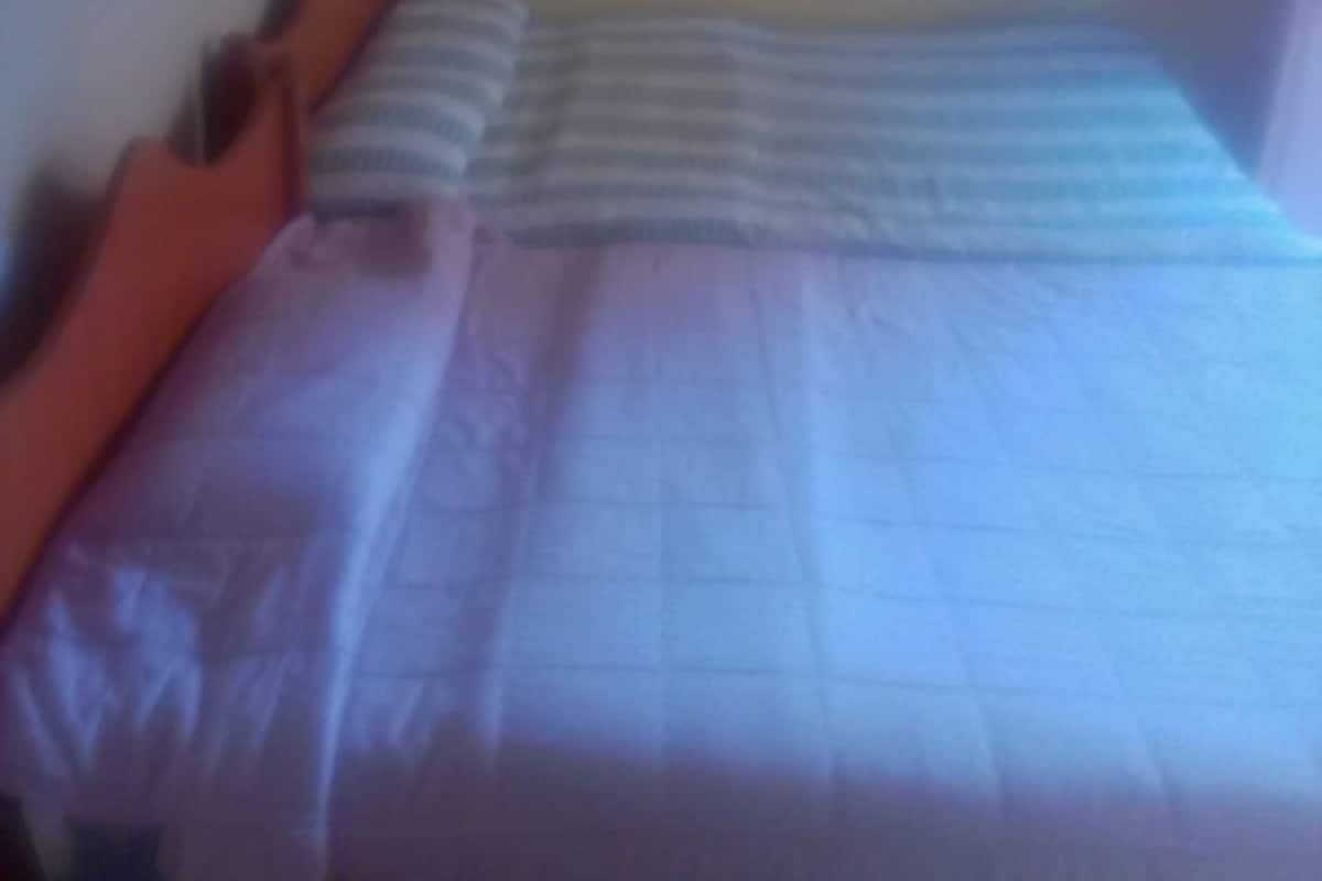 Quarto pequeno com uma cama de solteiro, colchão e almofadas simples.