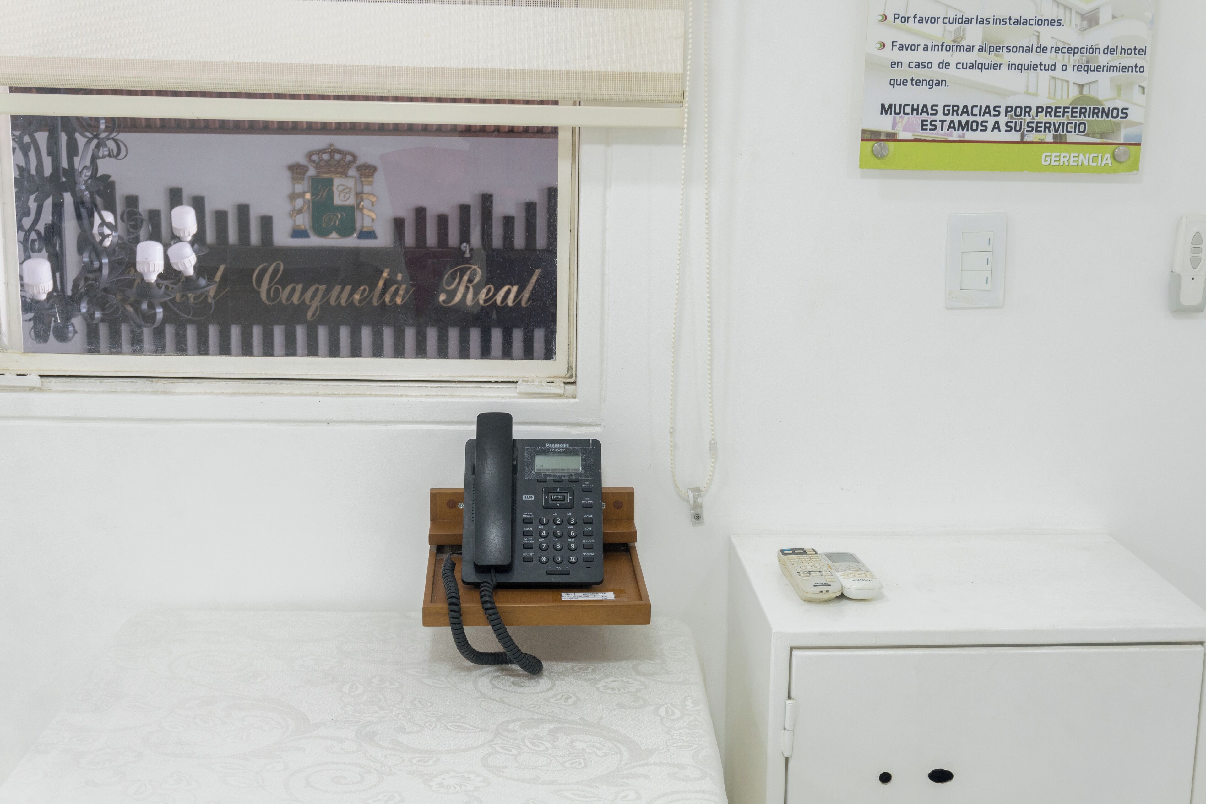 Uma área de recepção de hotel com um telefone, uma pequena mesa e uma placa na parede.