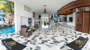 Um hall amplo com teto alto, um candelabro, um balcão de recepção e uma escadaria para um andar superior.