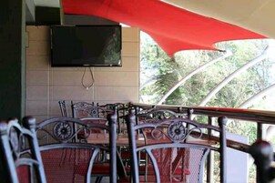 Restaurante com mesas ao ar livre, televisão montada na parede e toldo vermelho para dar sombra.