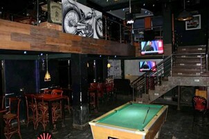 Mesa de bilhar em um ambiente com pouca luz, móveis de madeira e um grande mural de uma motocicleta na parede.