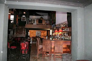 Uma área de bar com mobiliário de madeira, um balcão com garrafas e uma escada que leva a um andar superior.