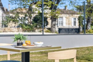 Uma mesa com tigela de cereais, copo de suco de laranja e um muffin em um dia ensolarado.
