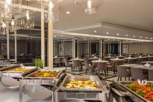 Uma área de refeições moderna com várias estações de buffet, arranjos de assentos e luminárias pendentes.