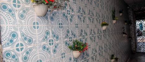 Paredes revestidas de azulejos com padrões geométricos e vários vasos de plantas.