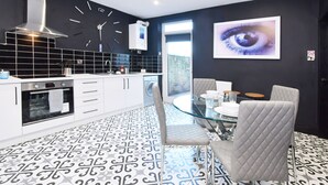 Cozinha moderna com painel de fundo preto, armários brancos e mesa de jantar de vidro com quatro cadeiras.
