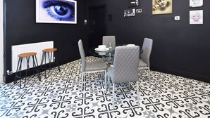 Uma área de refeições com piso estampado em preto e branco, uma mesa de vidro e duas cadeiras estofadas.