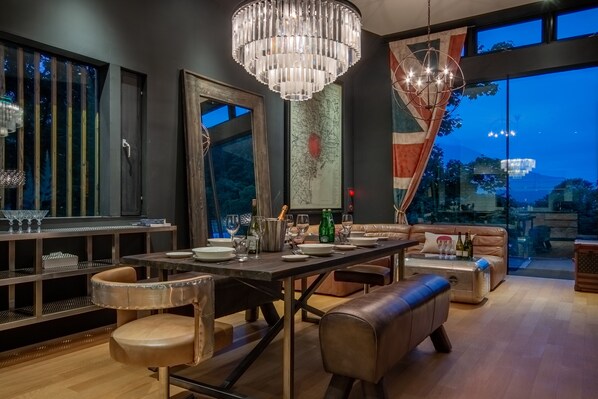 Uma área de jantar moderna com uma mesa grande, cadeiras de couro e um candelabro.