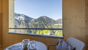 Interior em madeira com uma mesa, uma xícara e um copo de chá, com vista para uma paisagem montanhosa.