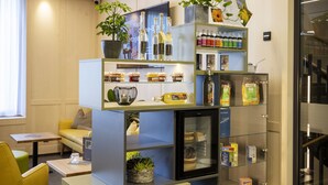 Um espaço de escritório moderno com uma mesa de recepção, prateleiras com diversos objetos, um vaso de planta e uma cadeira amarela.