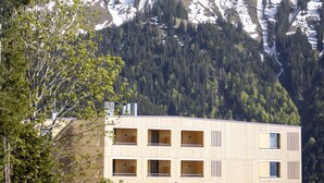 Um edifício moderno com várias varandas, com a paisagem de montanhas cobertas de neve e um céu claro ao fundo.
