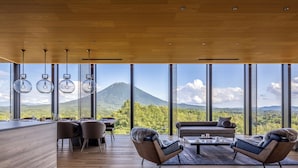 Interior moderno com teto de madeira, janelas amplas, área de refeições e assentos com vista para uma montanha.