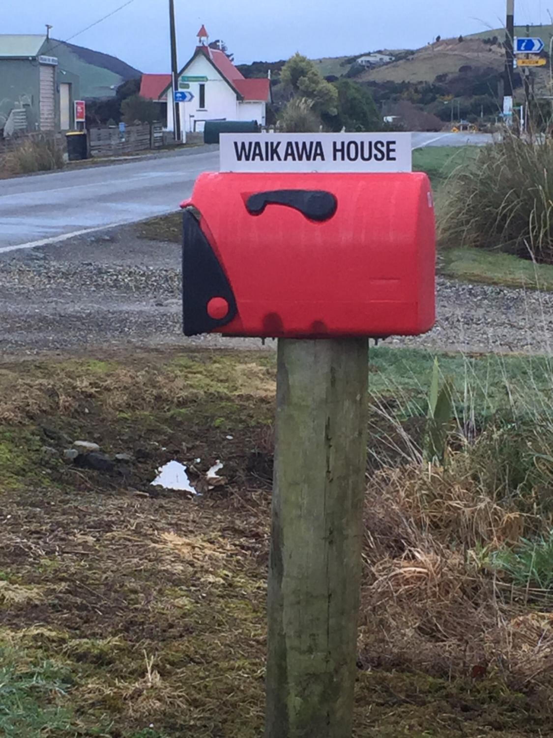 Uma caixa de correio com uma placa que diz "WAIKAWA HOUSE" fixada num poste de madeira.