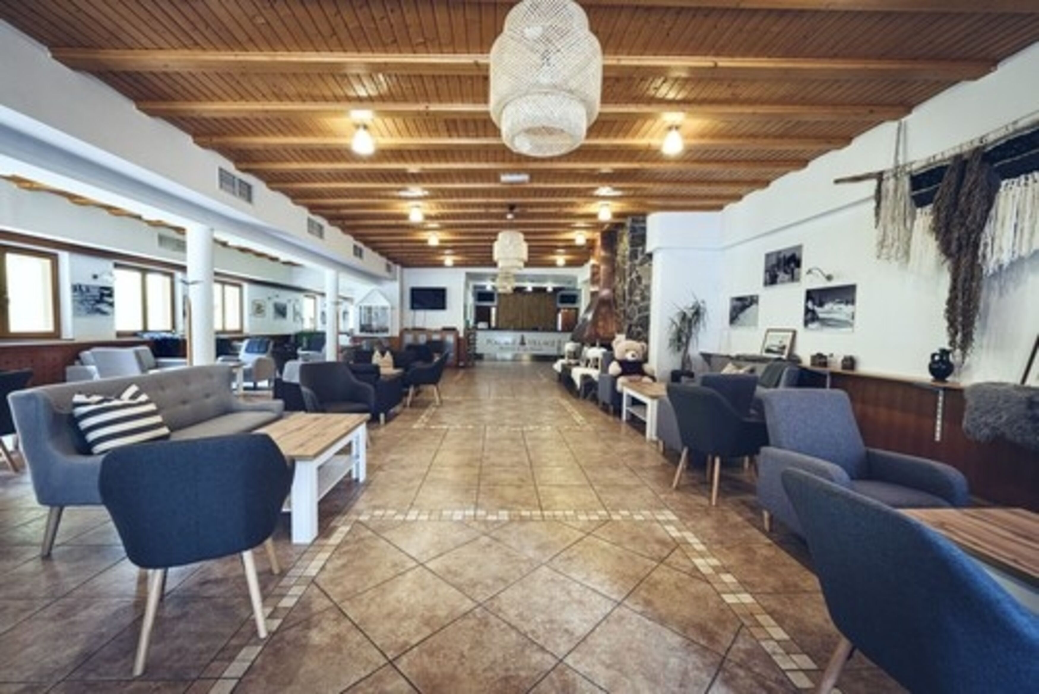 Um hall amplo com móveis modernos, teto de madeira e um lustre central.