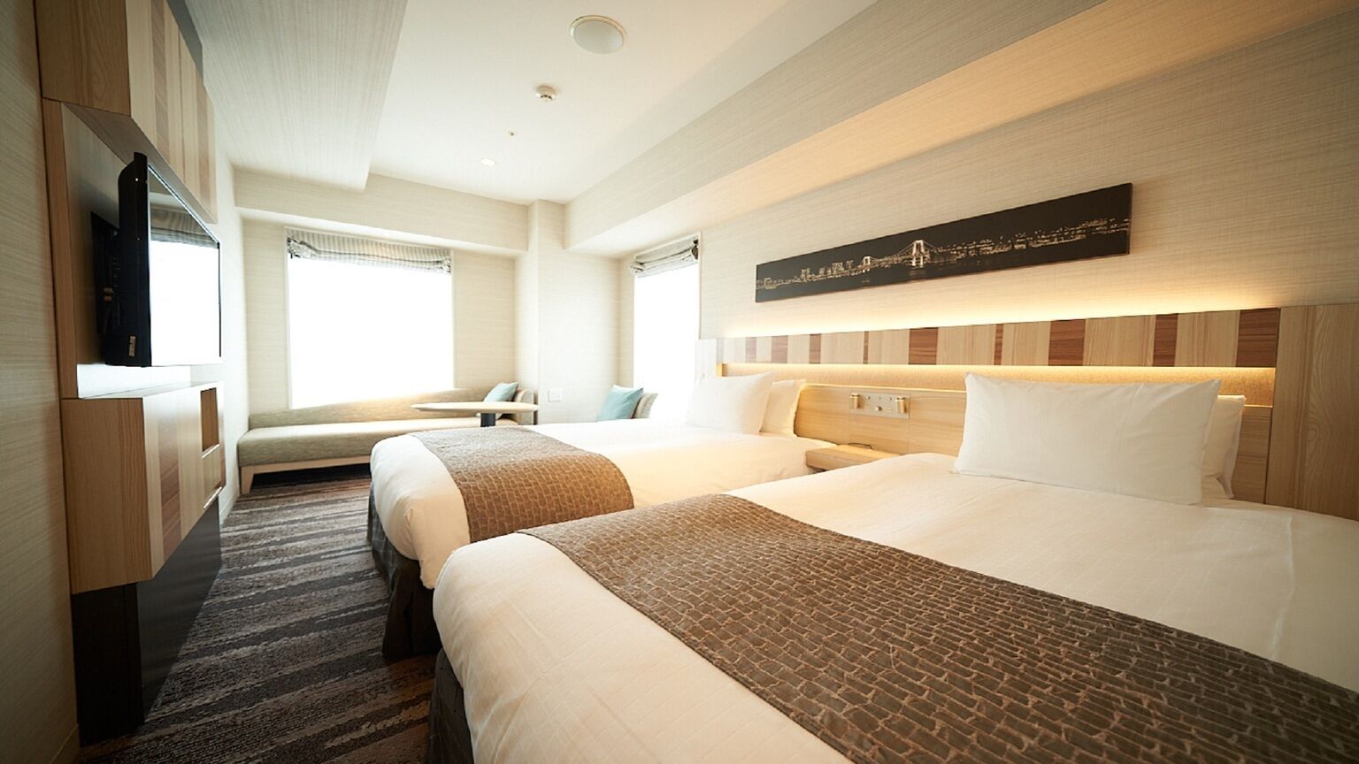 Quarto de hotel com duas camas, uma escrivaninha, uma cadeira e uma televisão.