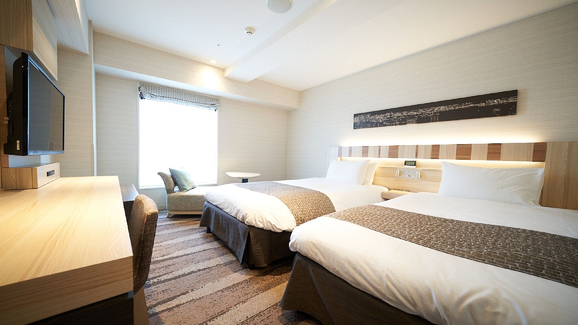 Quarto de hotel com duas camas, uma escrivaninha, uma cadeira, televisão e janela com cortinas.