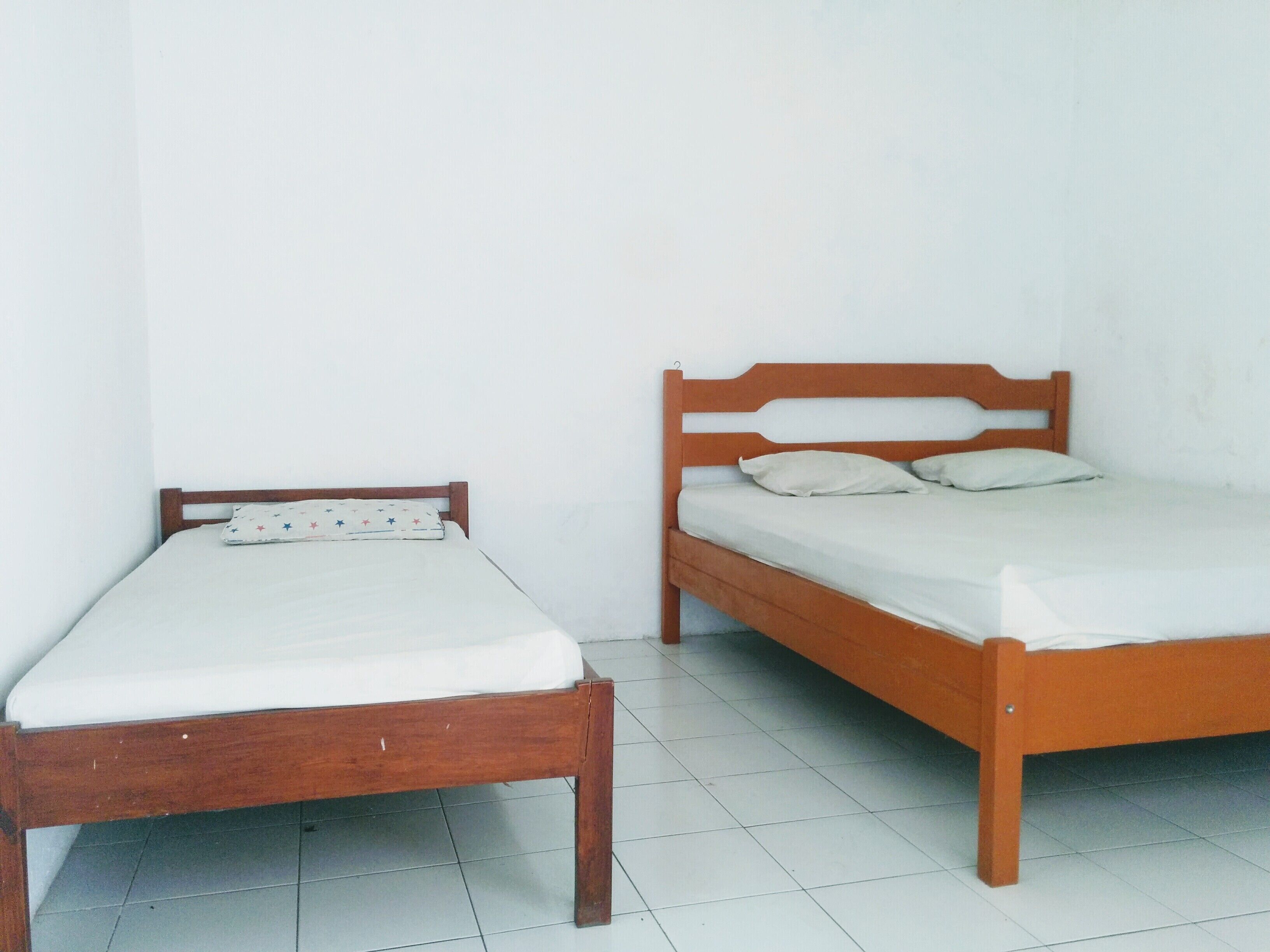 Duas camas de madeira com roupa de cama branca em quarto com paredes brancas e chão em azulejo.